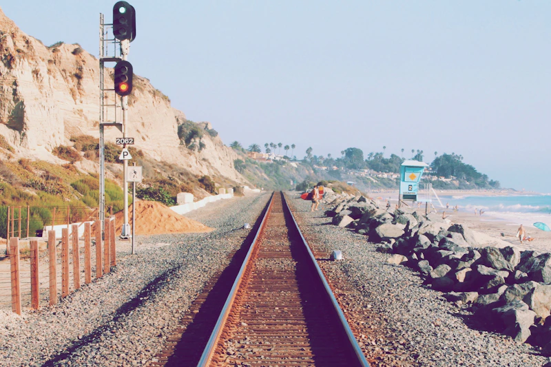 Railway tracks stretch along a rocky coastline with cliffs and a distant beach lifeguard tower.